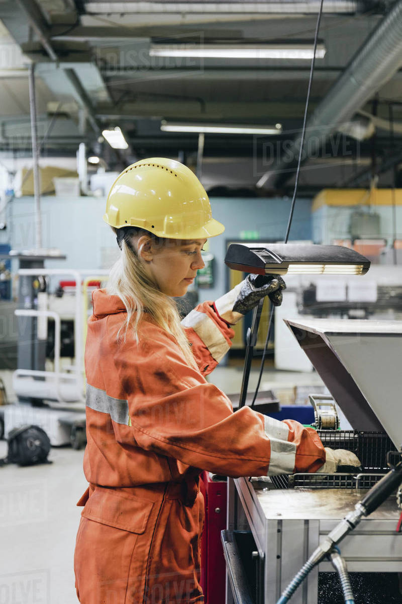 Young female industrial worker in uniform using manufacturing machinery ...