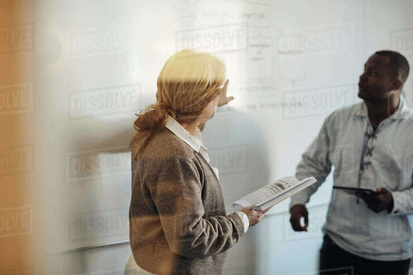 Side view of professor with book teaching diagram on whiteboard in ...
