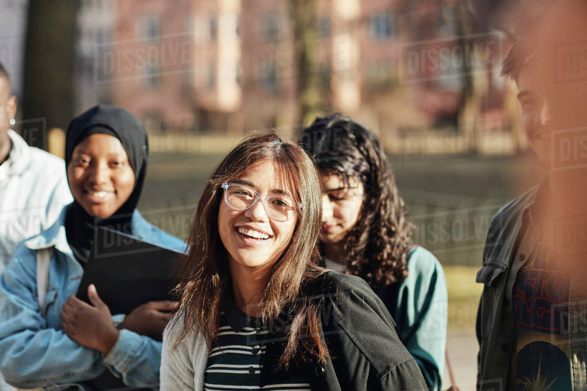 Portrait of smiling young female student with friends at university ...