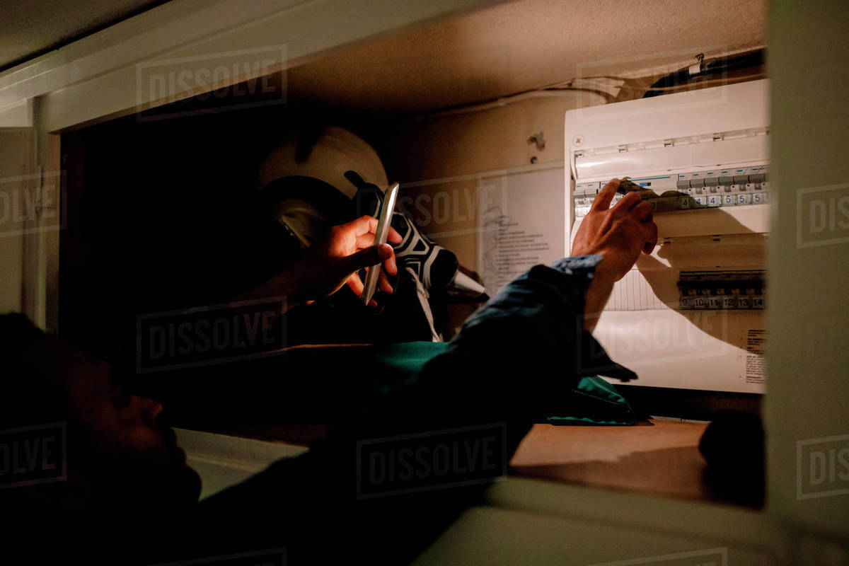 Man turning on switch from fuse box using smart phone torch during ...