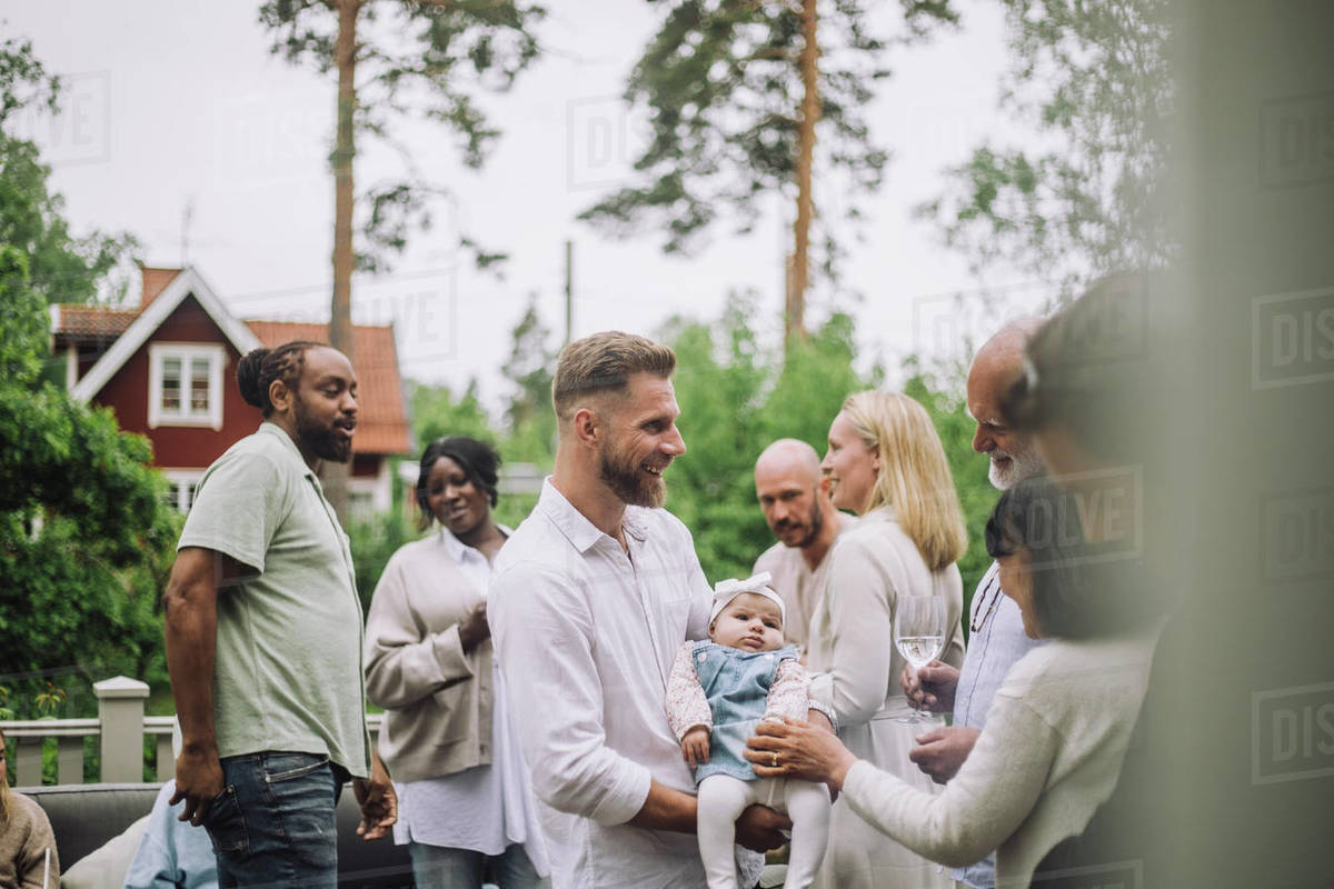 Smiling man introducing daughter to family members at dinner party ...