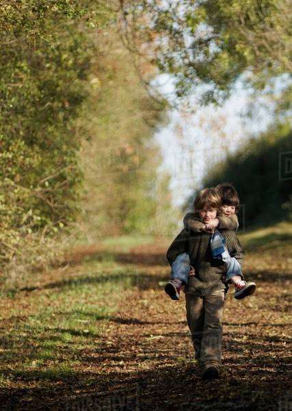 Boy carrying young child in countryside - Stock Photo - Dissolve