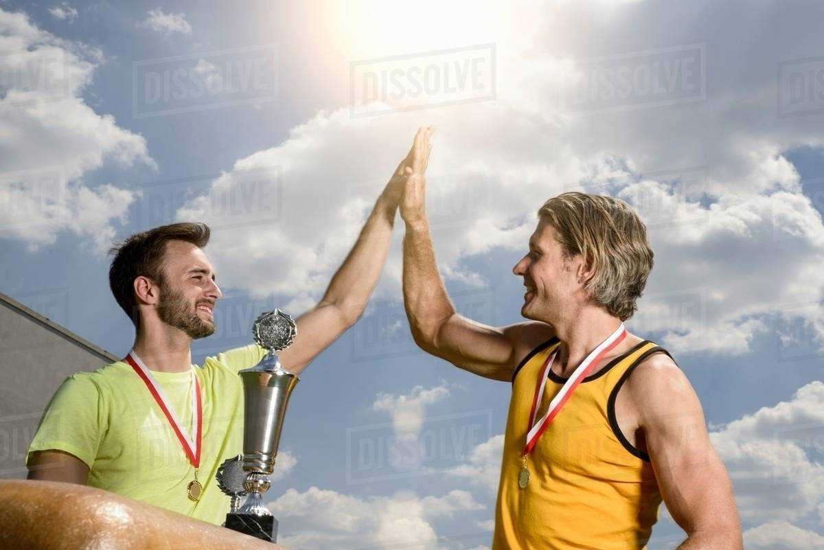 Two male gymnasts with trophies giving each other high five - Stock ...