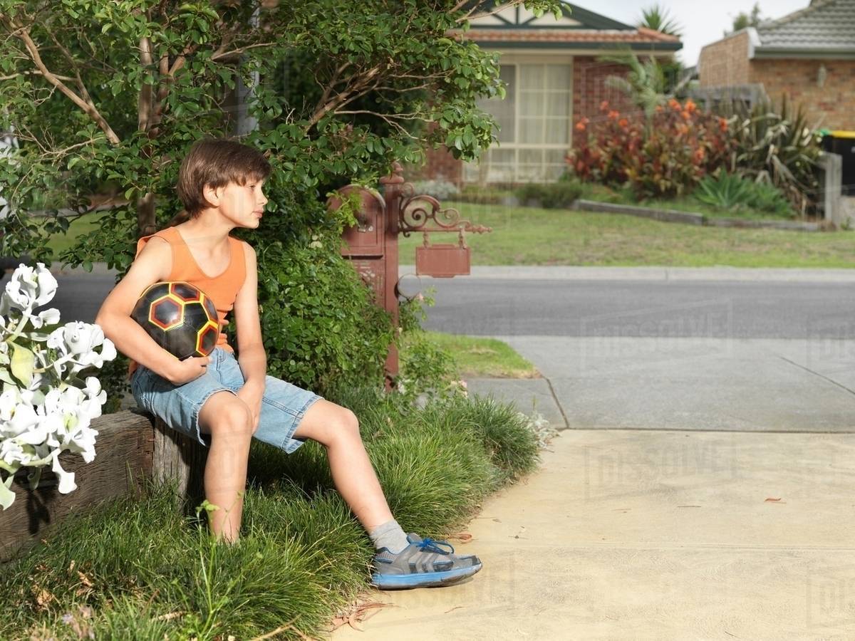 Sullen boy sitting on suburban wall holding soccer ball - Royalty-free ...
