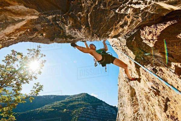 Female climber, climbing out of a cave with an old quarry in the ...
