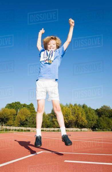 Boy with medals Jumping on Race Track - Stock Photo - Dissolve