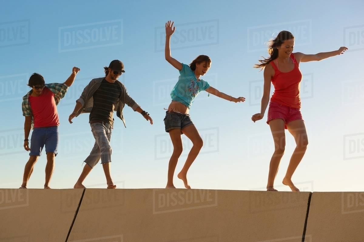 Young people balancing on wall - Stock Photo - Dissolve