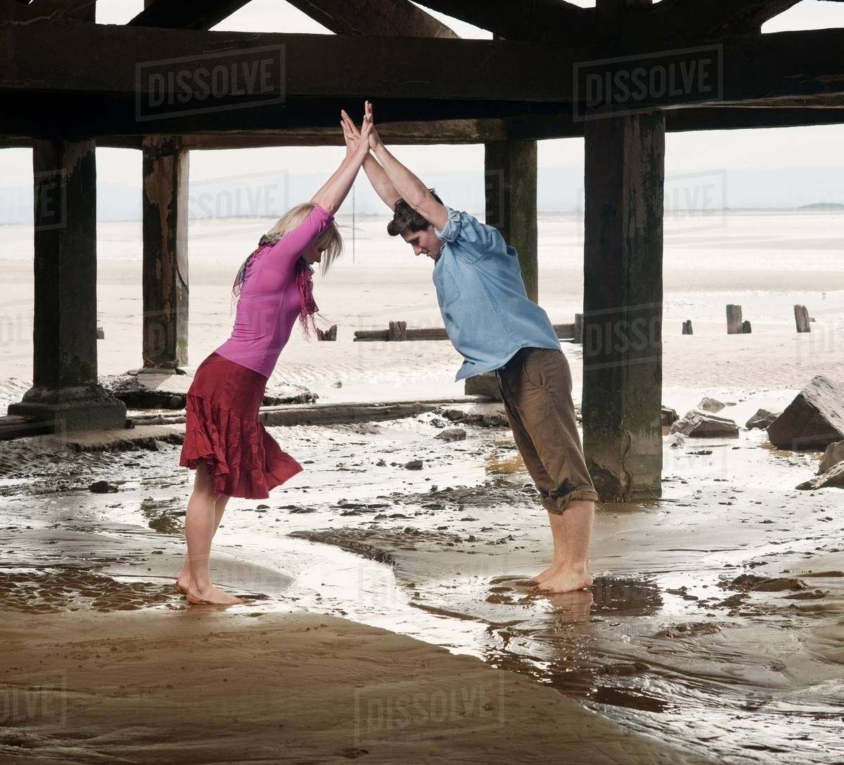 Couple reaching over stream on beach - Royalty-free Stock Photo | Dissolve