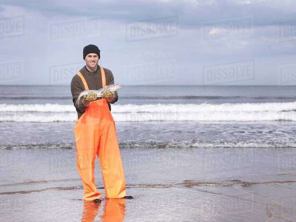 Fisherman on shore holding fish - Stock Photo - Dissolve