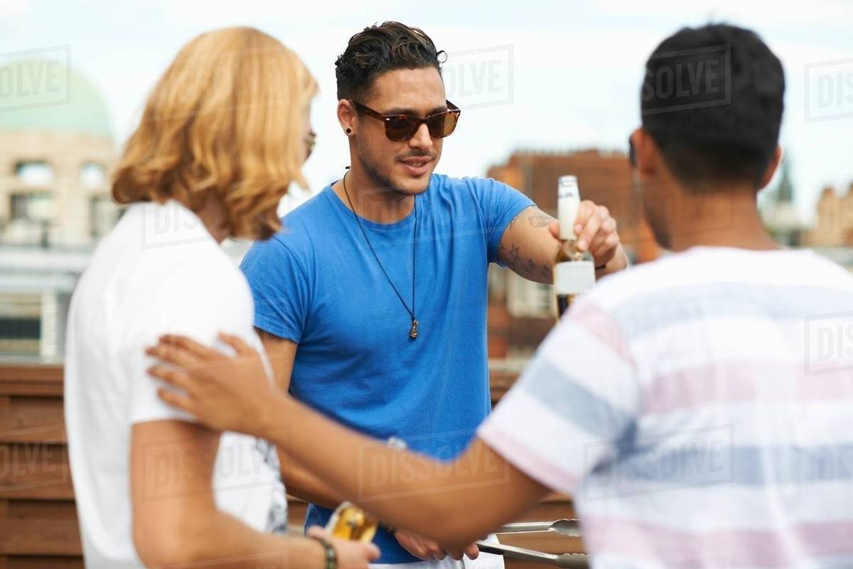 Three male friends handing out bottled beer at rooftop party - Royalty ...