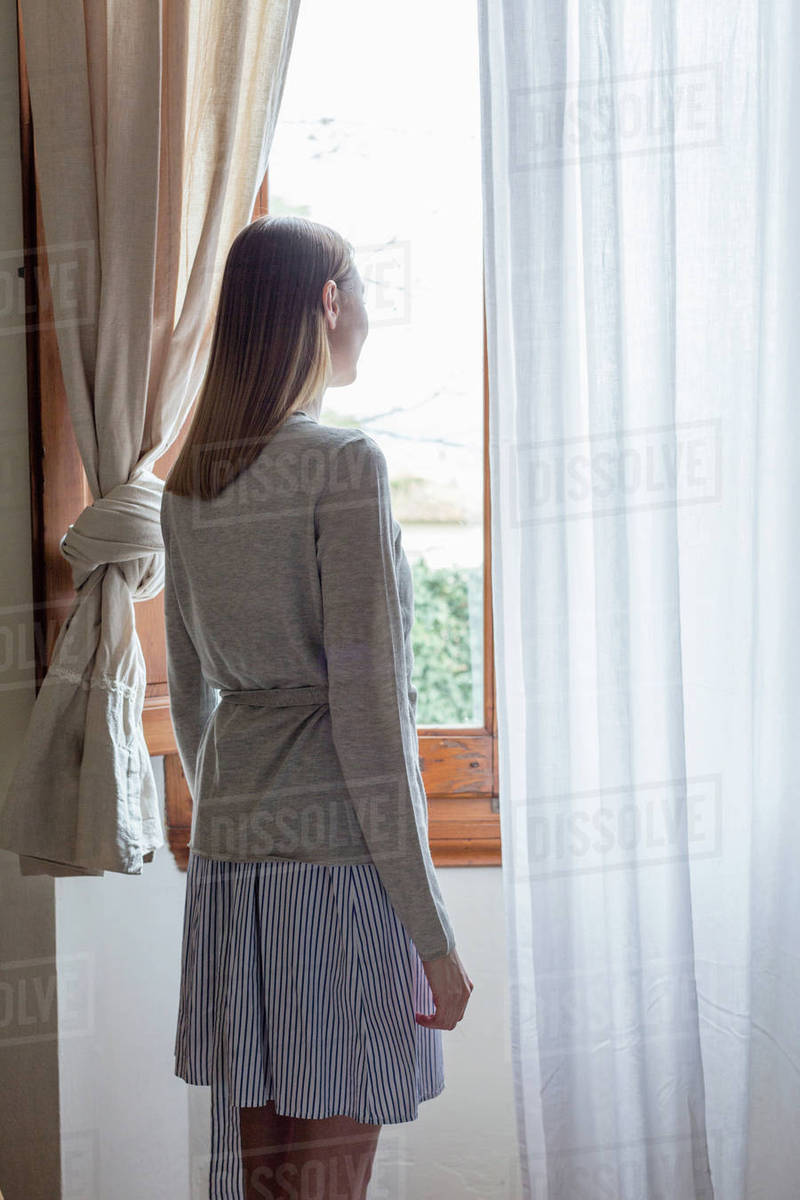 Rear view of woman standing looking out of window - Stock Photo - Dissolve