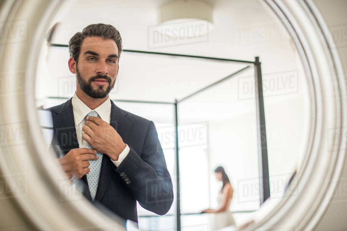 Mirror reflection of young businessman adjusting shirt and tie in hotel ...