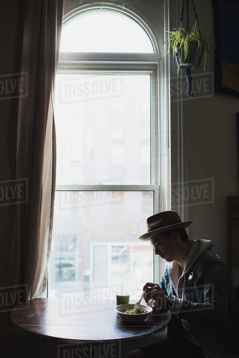 Young man sitting at table by window, eating healthy meal - Royalty ...
