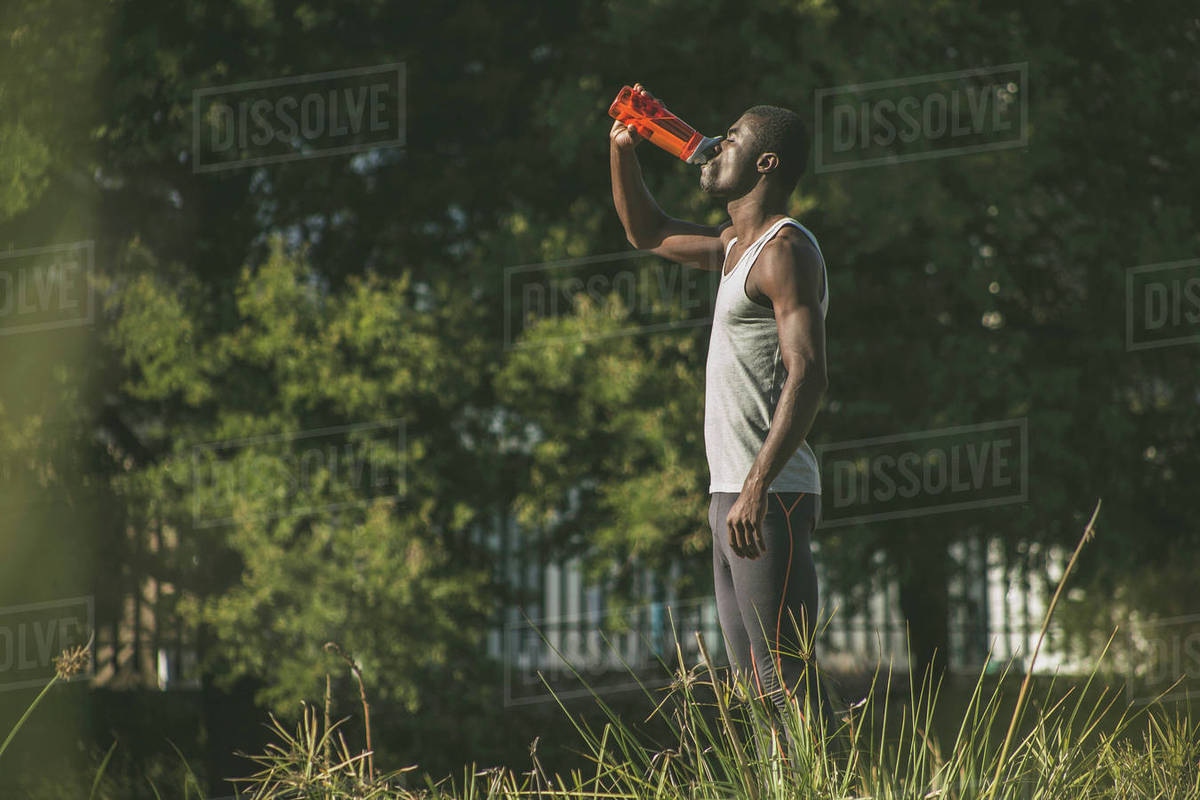 Side view man in field drinking from plastic bottle - Royalty-free ...