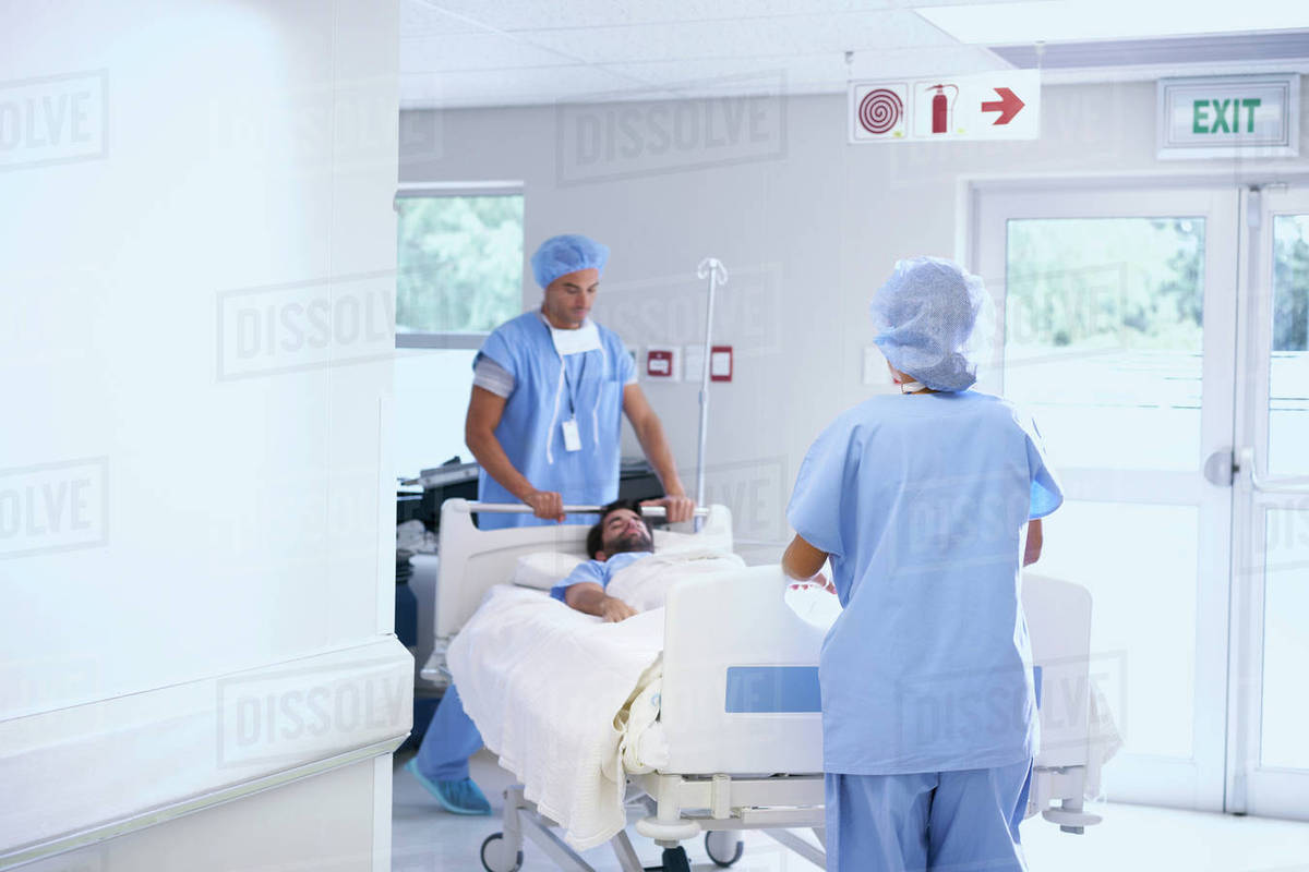 Doctors wearing surgical scrubs pushing patient on hospital bed ...