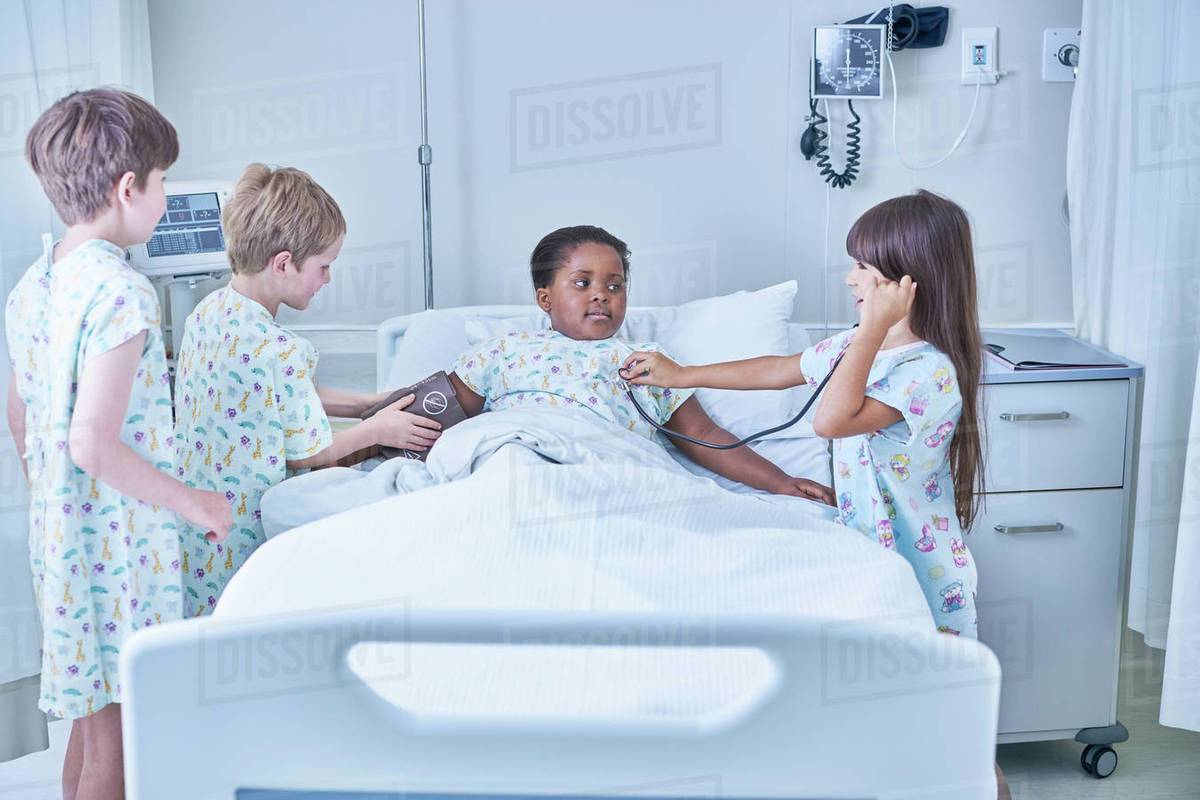 Girl and boy patients playing at treating friend in bed on hospital ...