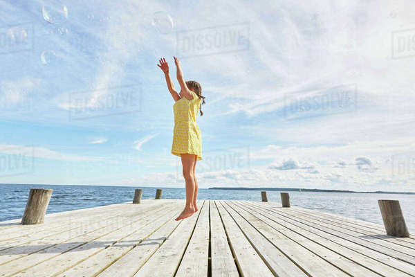 Young girl on wooden pier, jumping to reach bubbles - Stock Photo ...