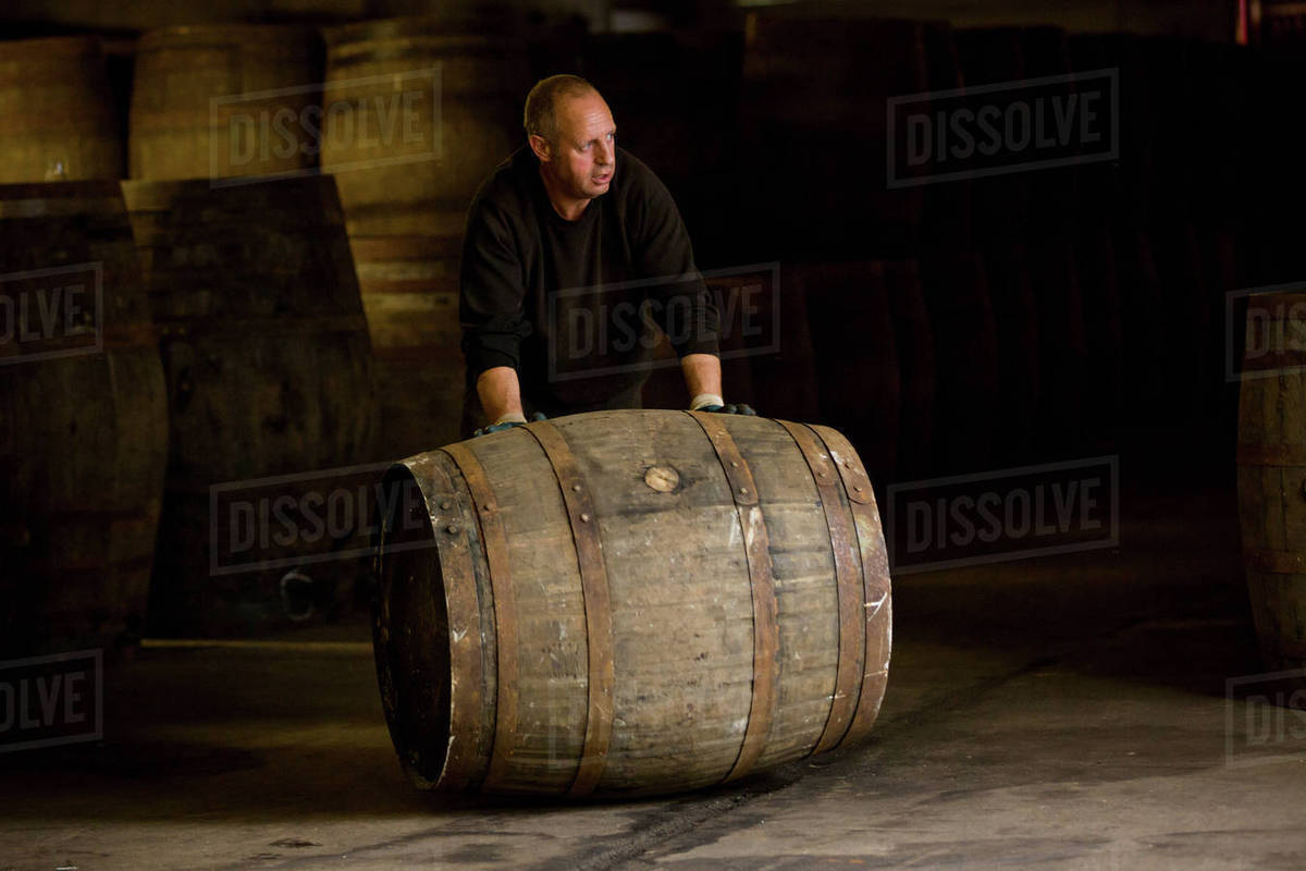 Worker rolling whisky cask in whisky distillery - Stock Photo - Dissolve