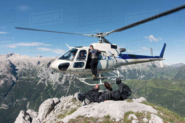 Male and female BASE jumping team exiting helicopter on top of mountain ...