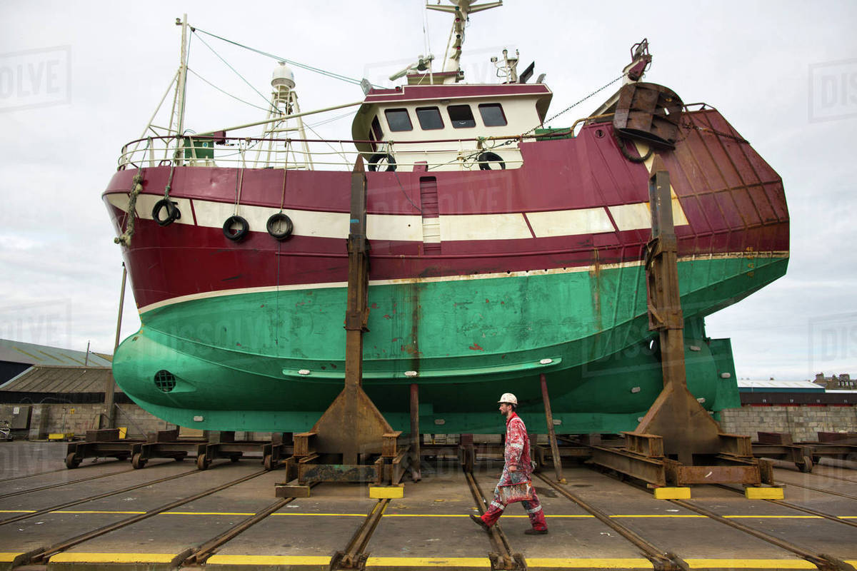 Male ship painter walking in front of fishing boat on drydock - Stock ...