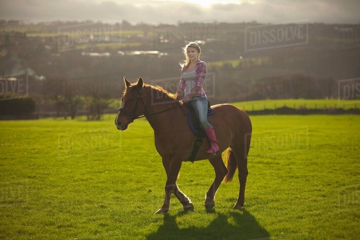 Teenage girl riding horse in field - Stock Photo - Dissolve