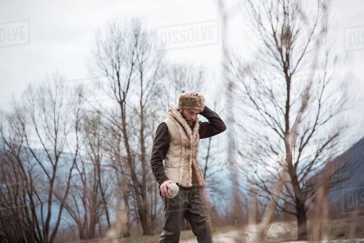 Mid adult man wearing trapper hat by trees - Stock Photo - Dissolve