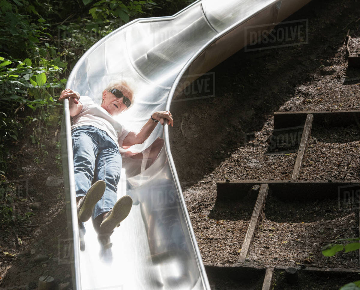 Woman sliding down playground slide - Stock Photo - Dissolve