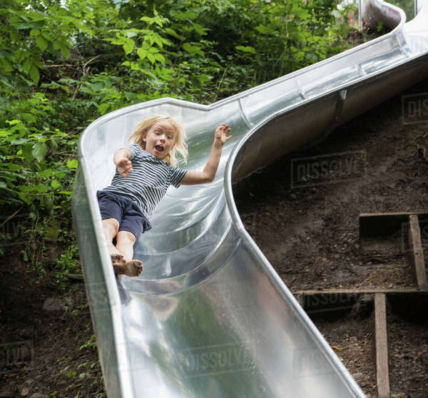 Boy sliding down playground slide - Stock Photo - Dissolve