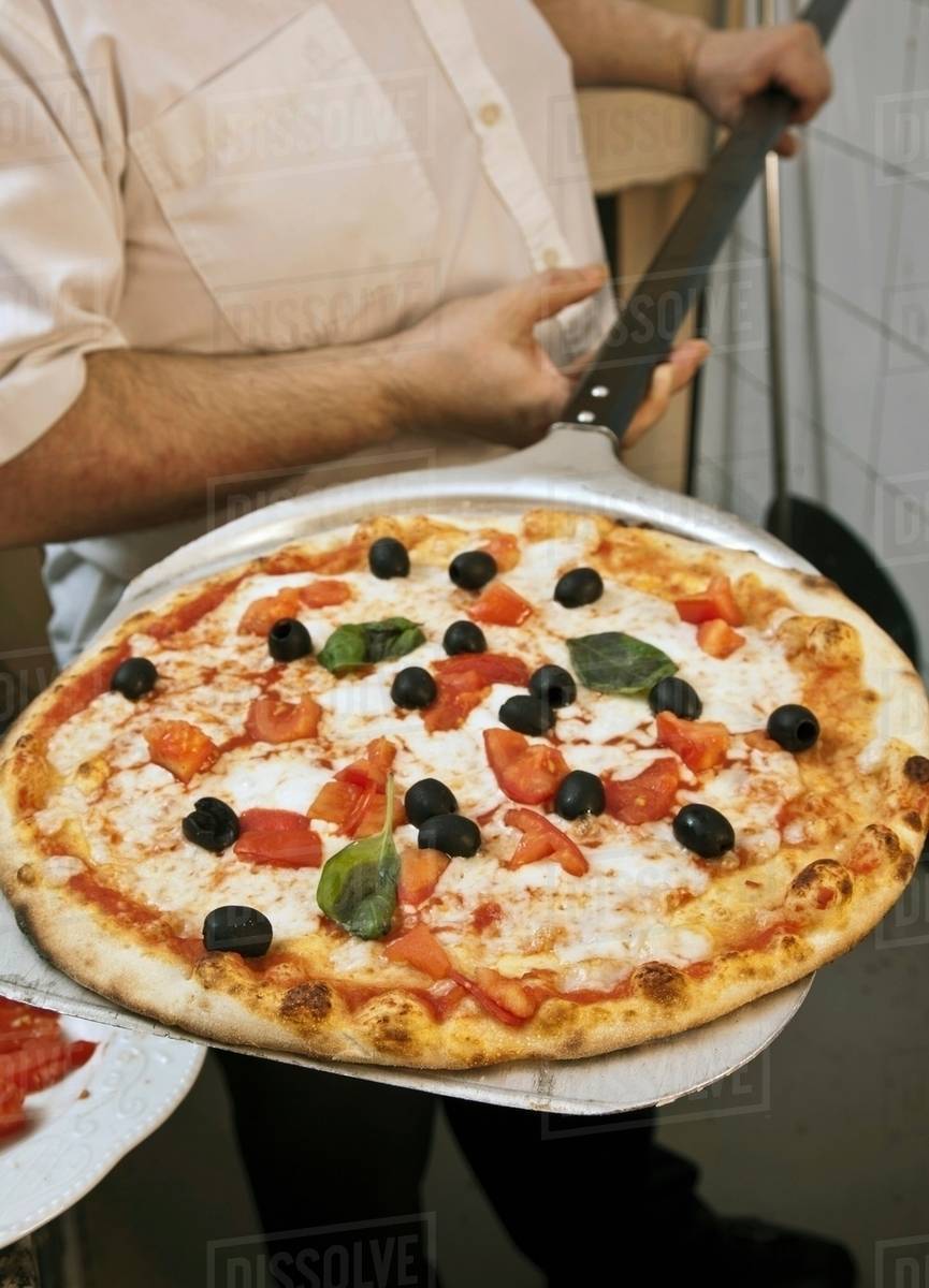 Chef holding pizza on spatula - Stock Photo - Dissolve