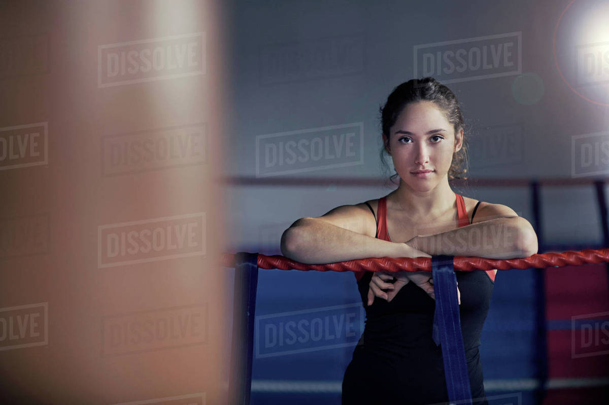 Portrait of young female boxer leaning on boxing ring ropes - Royalty ...