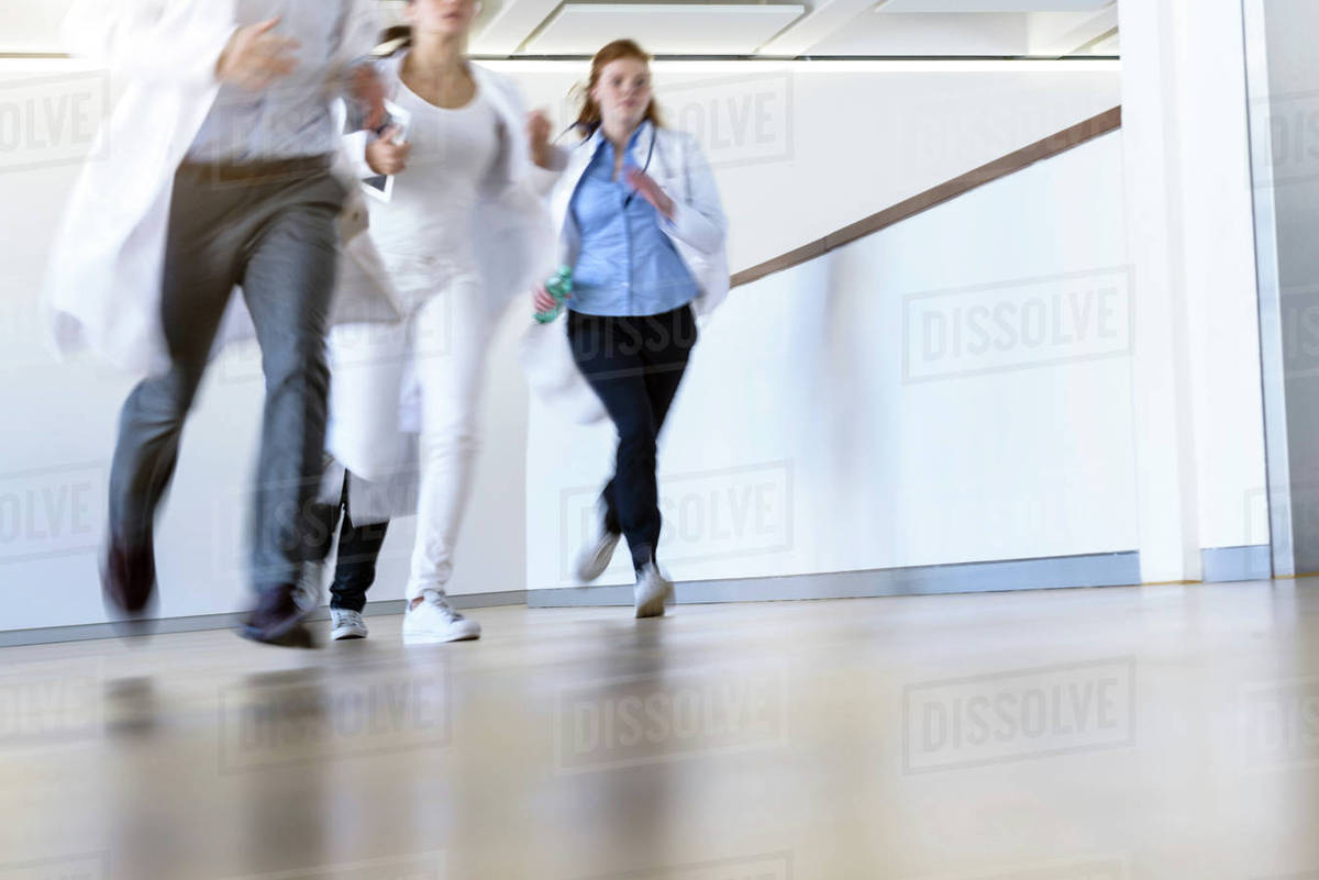 Male and female doctors running along hospital corridor - Stock Photo ...