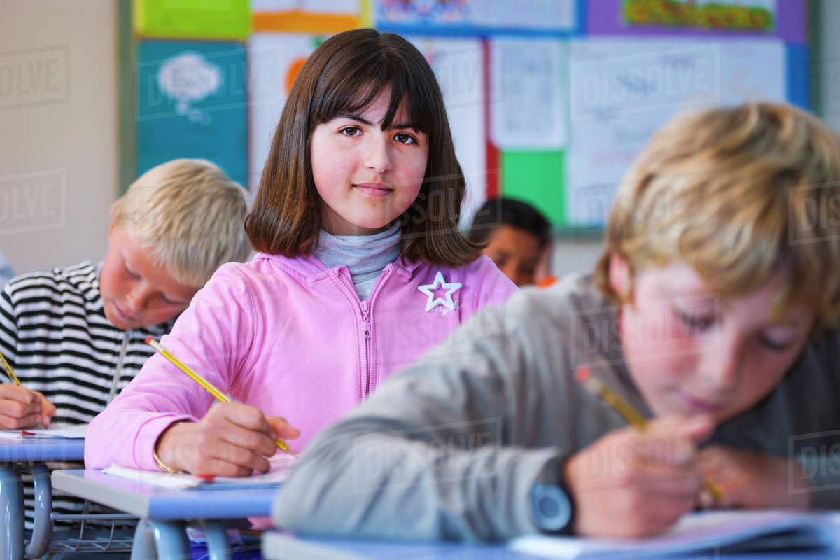 Portrait of girl in classroom, sitting at desk, doing classwork ...
