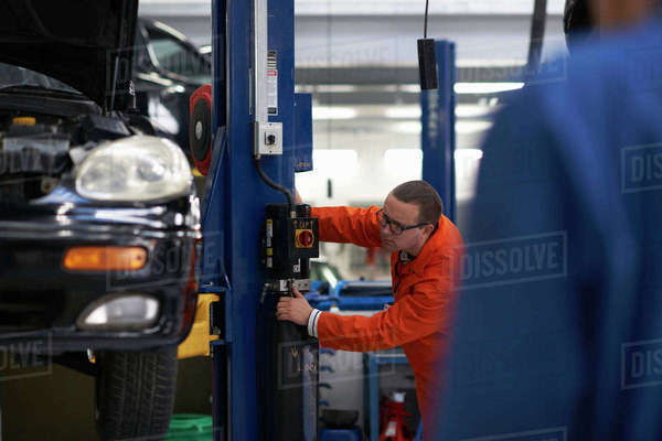 College mechanic student operating car lift in repair garage - Royalty ...