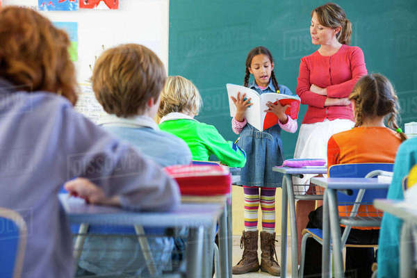 Primary schoolgirl reading at front of classroom - Royalty-free Stock ...