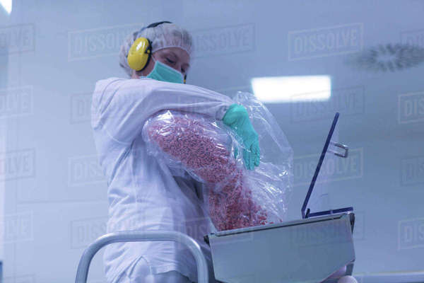 Worker pouring tablets into sorting machine in pharmaceutical plant ...