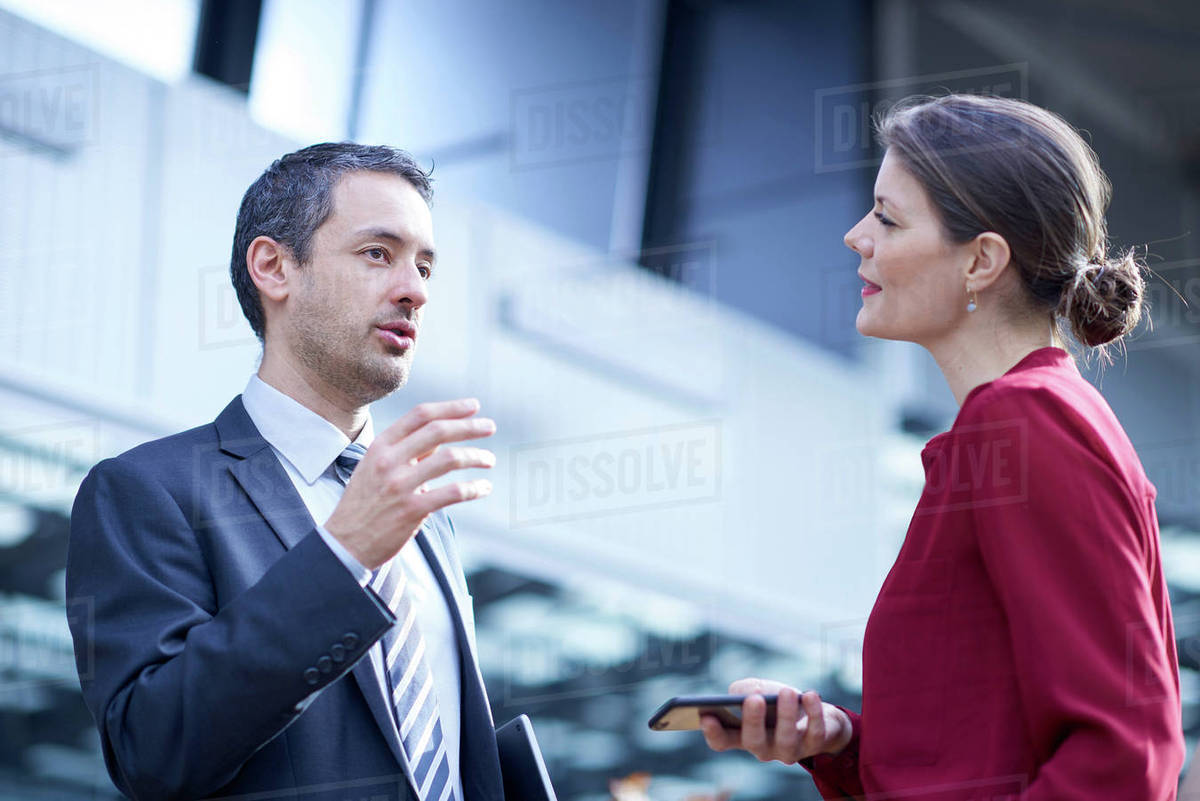 Businessman and woman talking in office atrium - Royalty-free Stock ...