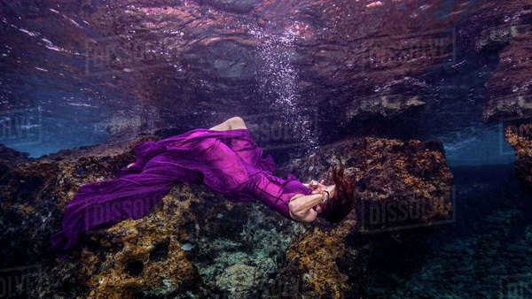 Woman arching backwards, draped in sheer purple fabric, underwater view ...