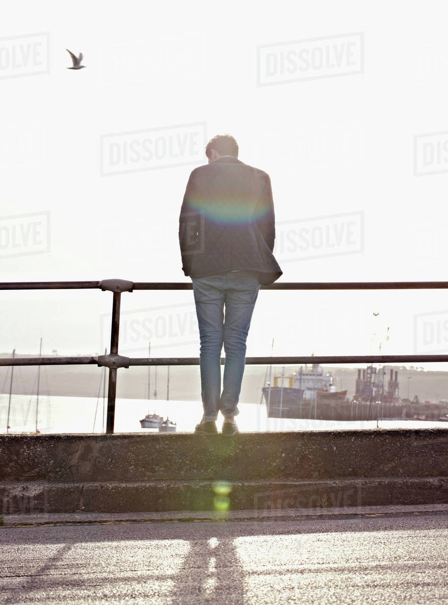 Man peering over railing of harbor - Stock Photo - Dissolve