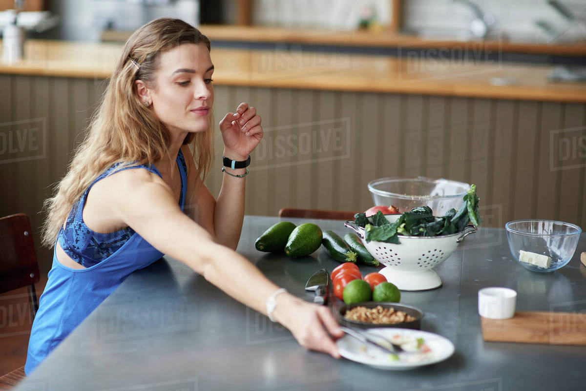 Young woman at kitchen table with finished salad plate - Royalty-free ...