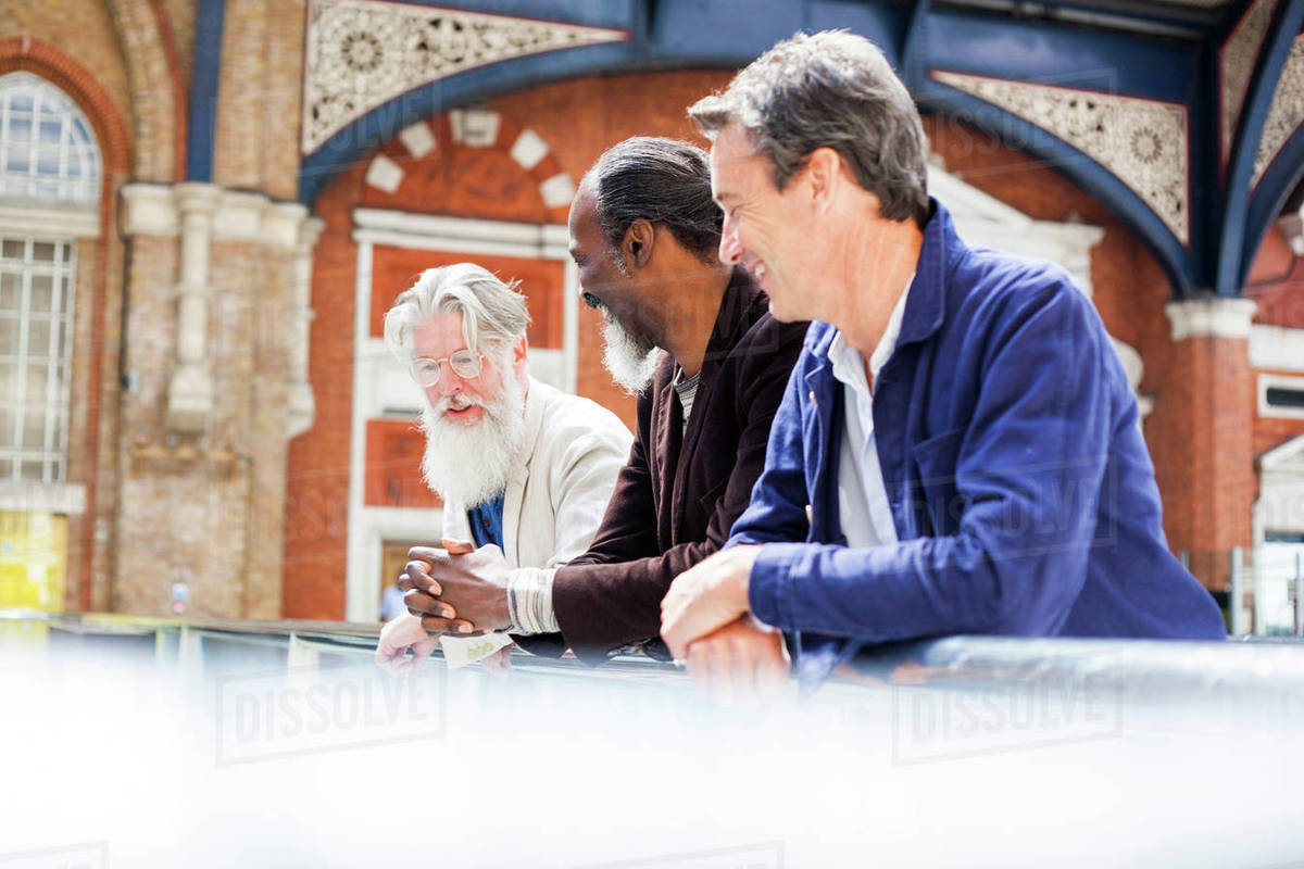 Three mature men at train station, standing together, talking - Stock ...