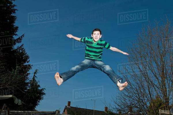 Smiling boy jumping for joy outdoors - Stock Photo - Dissolve