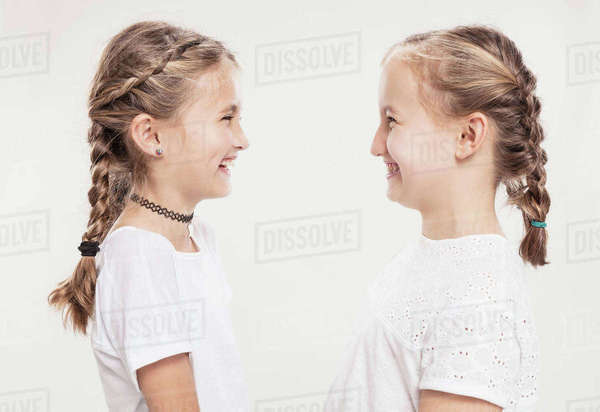 Studio portrait of two girls with hair plaits face to face, head and ...