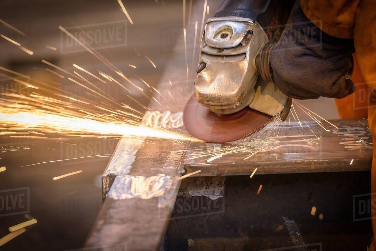 Worker grinding metal construction in marine fabrication factory ...