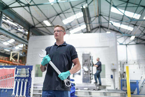 Engineer holding large spanner in gearbox factory - Stock Photo - Dissolve