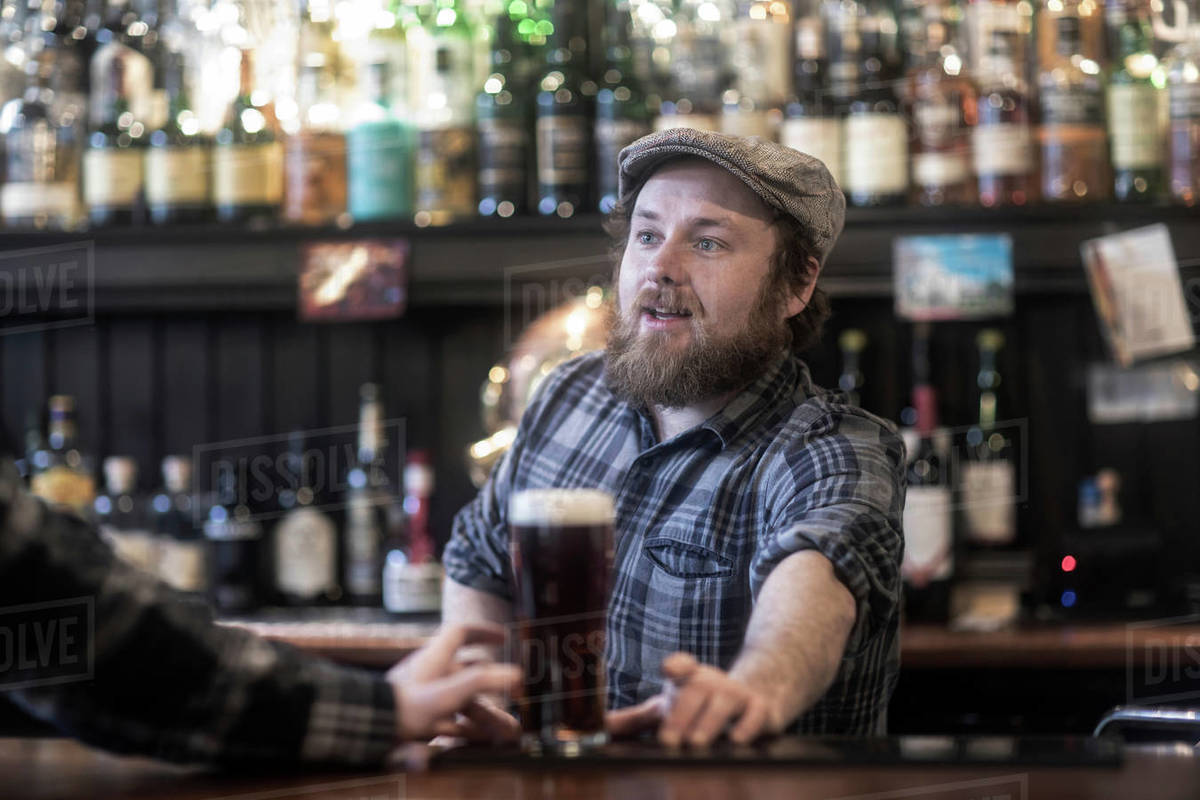 Barman serving beer to customer at bar in traditional Irish public ...
