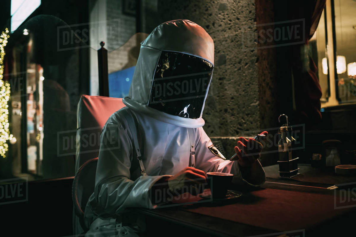 Astronaut using smartphone at sidewalk cafe - Stock Photo - Dissolve