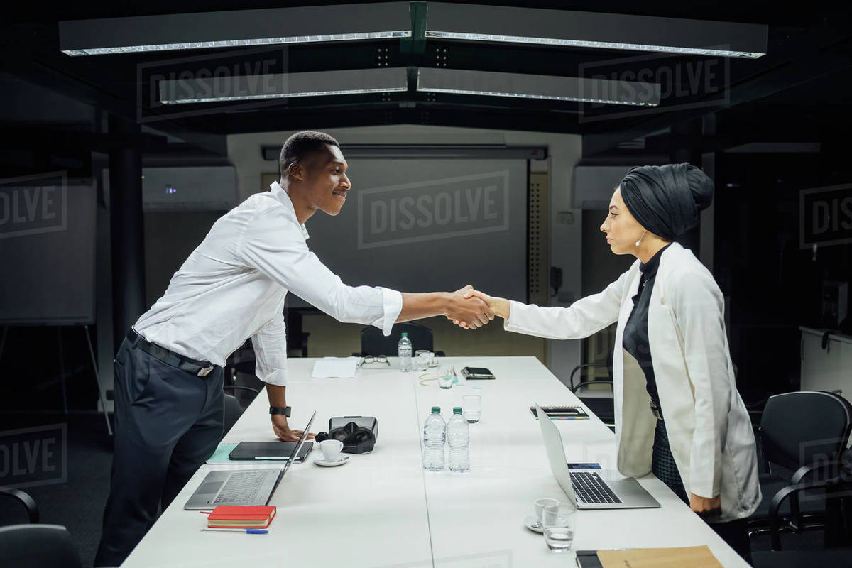 Businessman and woman shaking hands over conference table - Royalty ...