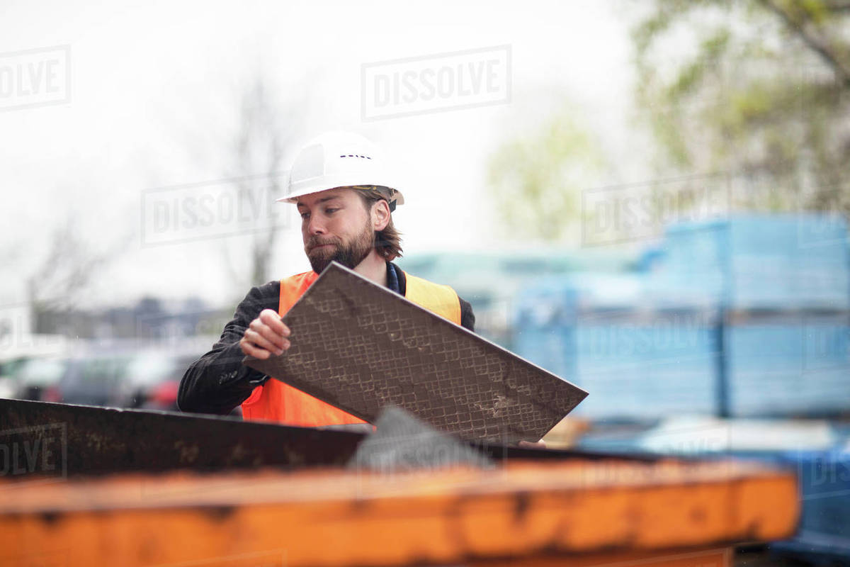 Mid adult male construction worker putting waste into waste skip ...