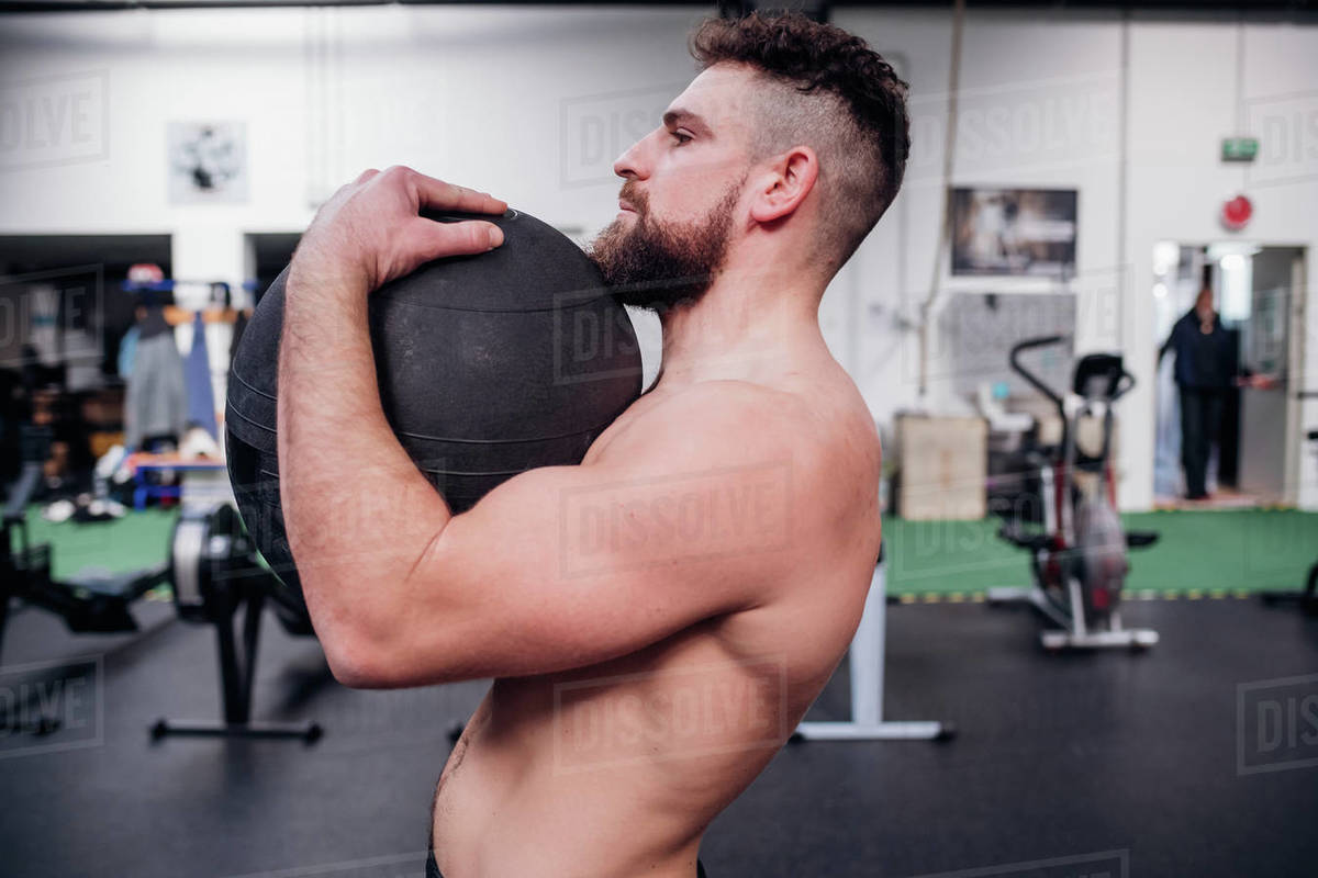 Young man training, lifting atlas ball in gym, side view - Royalty-free ...
