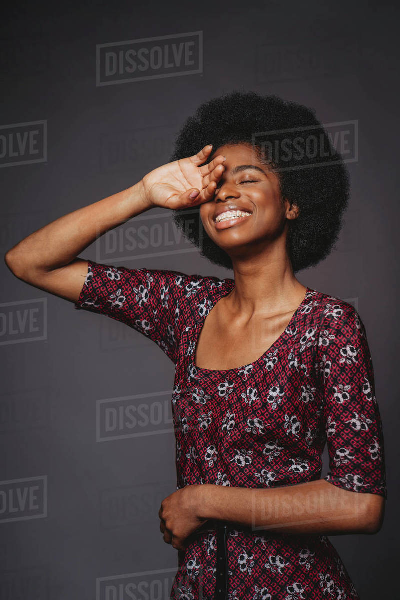 Young woman with afro hair covering eye and smiling, grey background ...